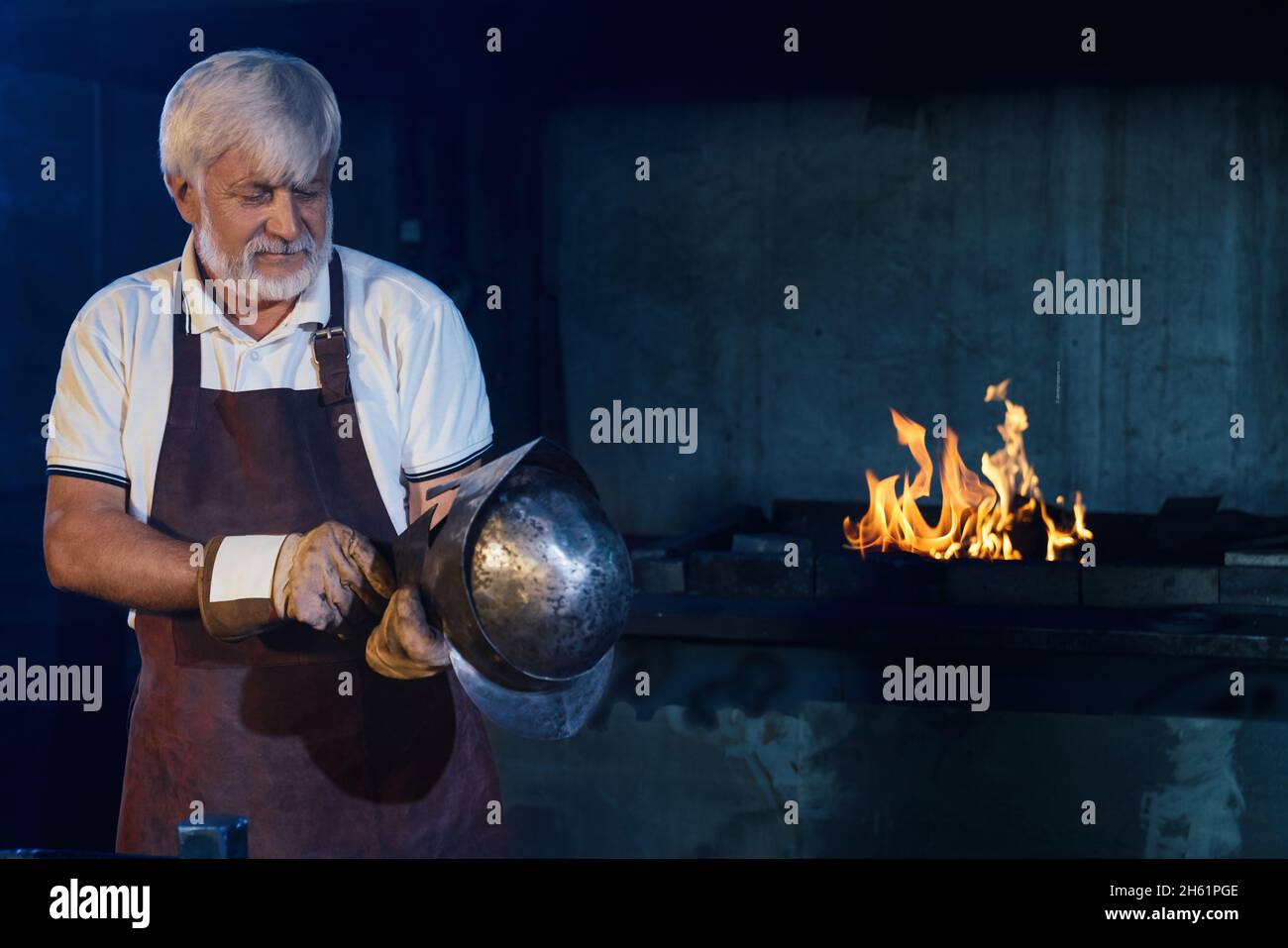 Skillful aged craftsman in protective apron and gloves making gladiator ...
