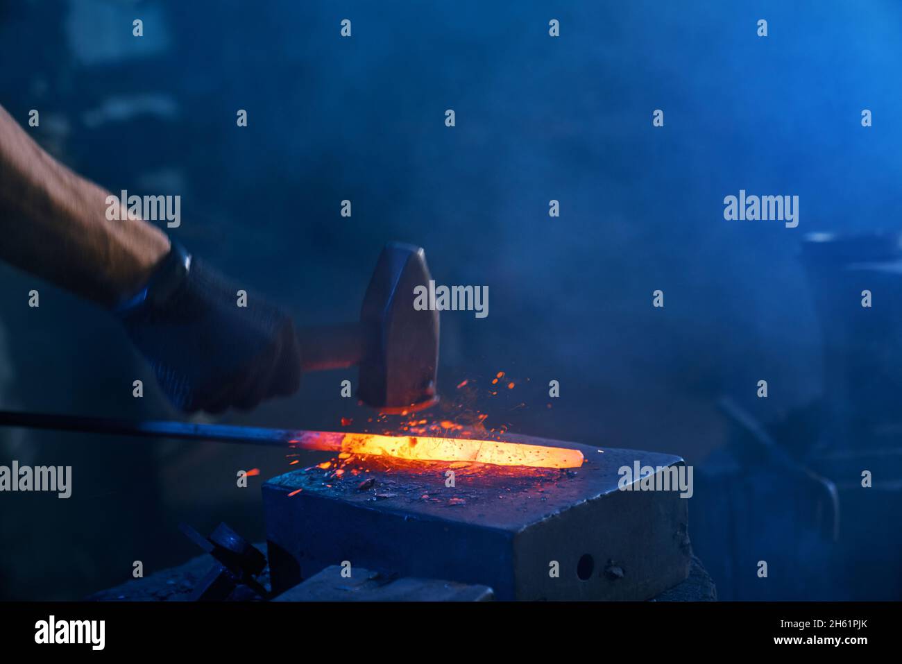 Close up of strong male hands and safety gloves forging molten metal on ...