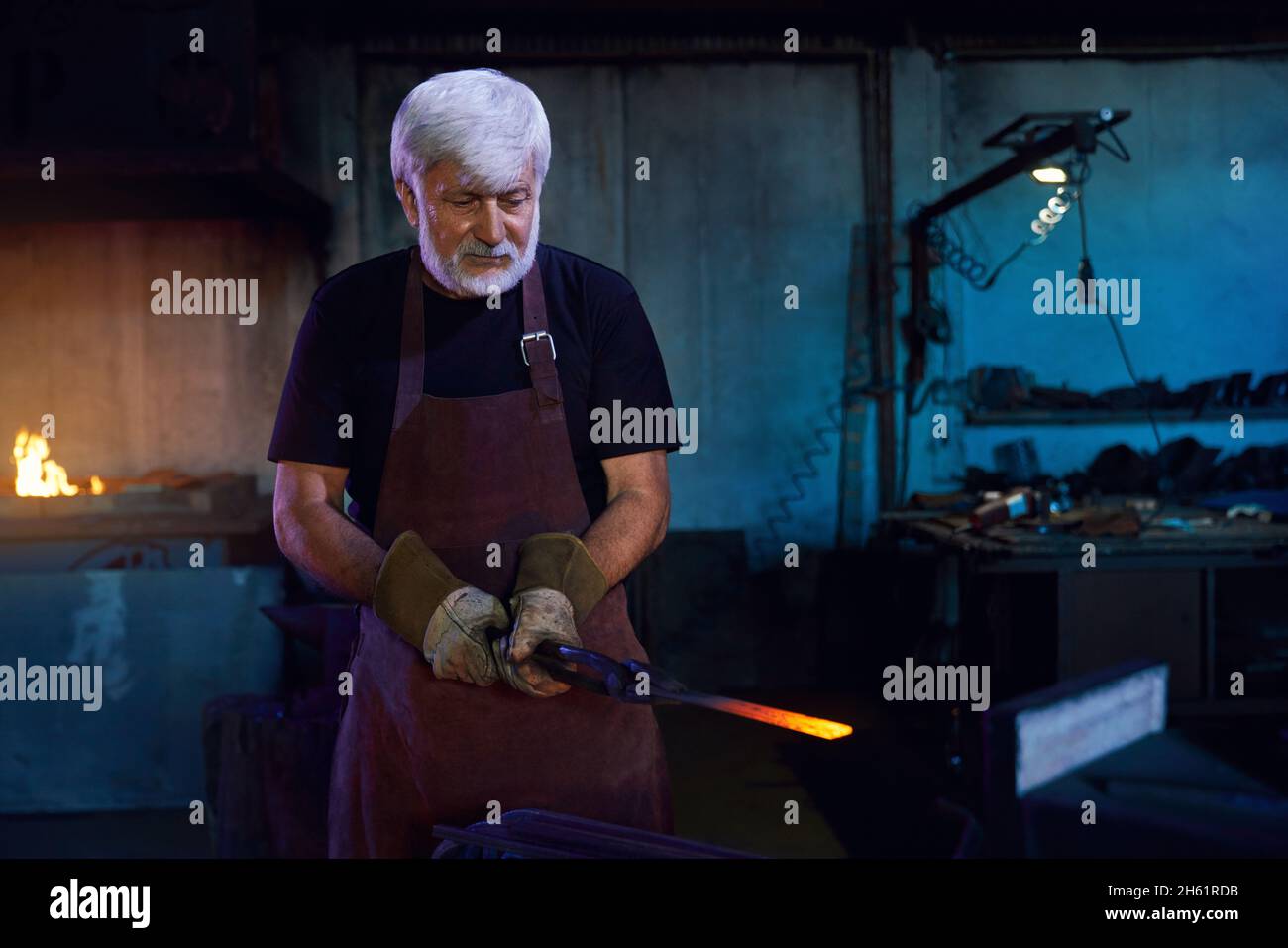 Caucasian aged man in safety apron and gloves working with molten metal ...