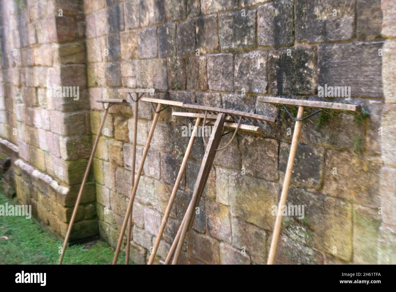 Wooden lawn rakes leaning against a stone wall at Fountains Abbey ...