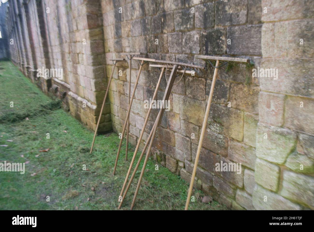 Wooden lawn rakes leaning against a stone wall at Fountains Abbey ...