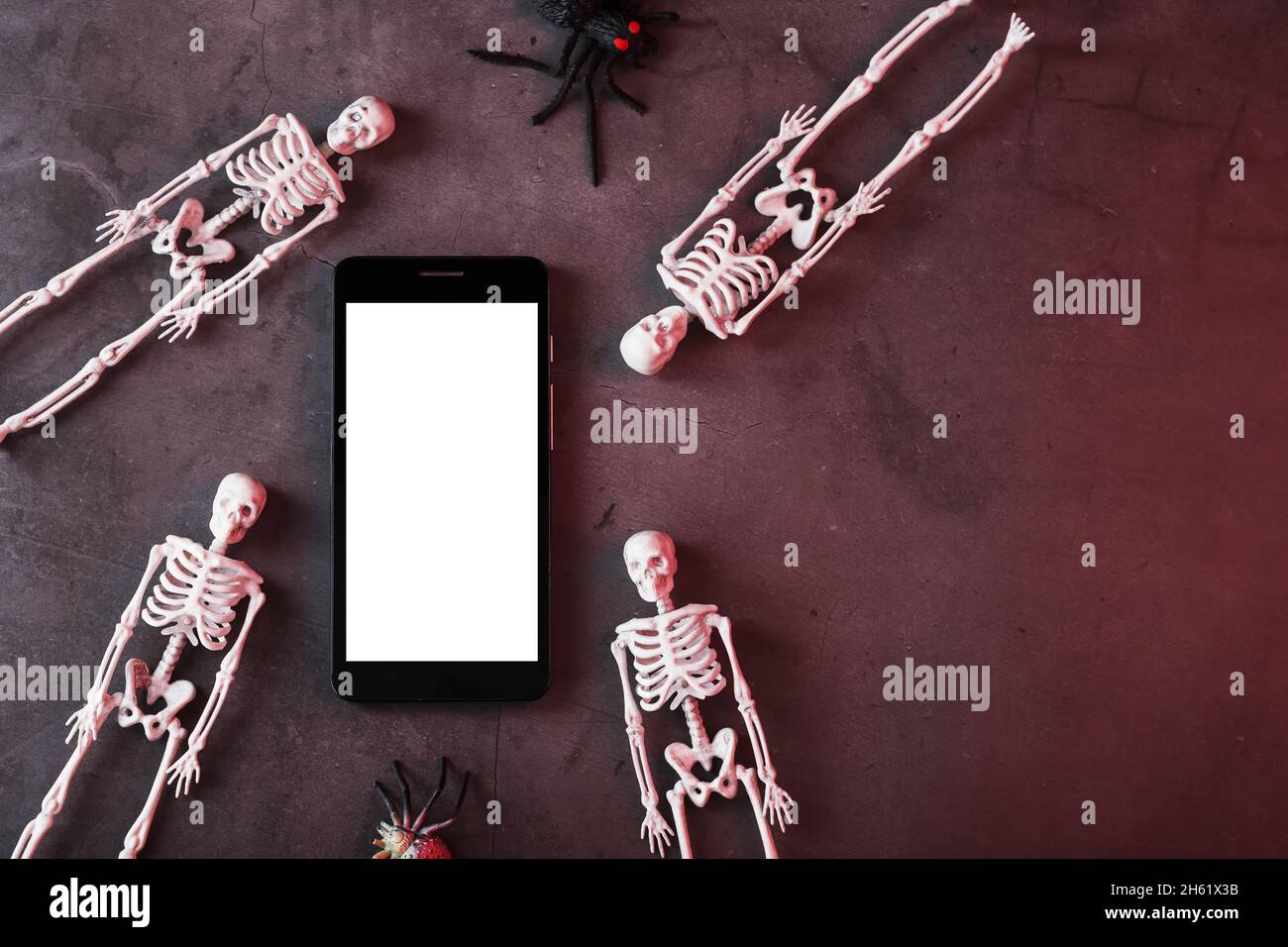 Decorative skeletons lie near the smartphone on a dark background ...