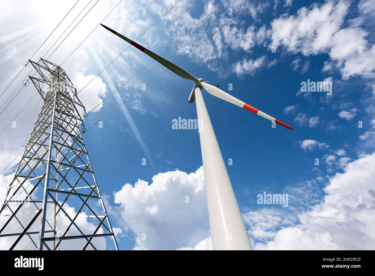White and red wind turbine and high voltage tower (power line) against ...