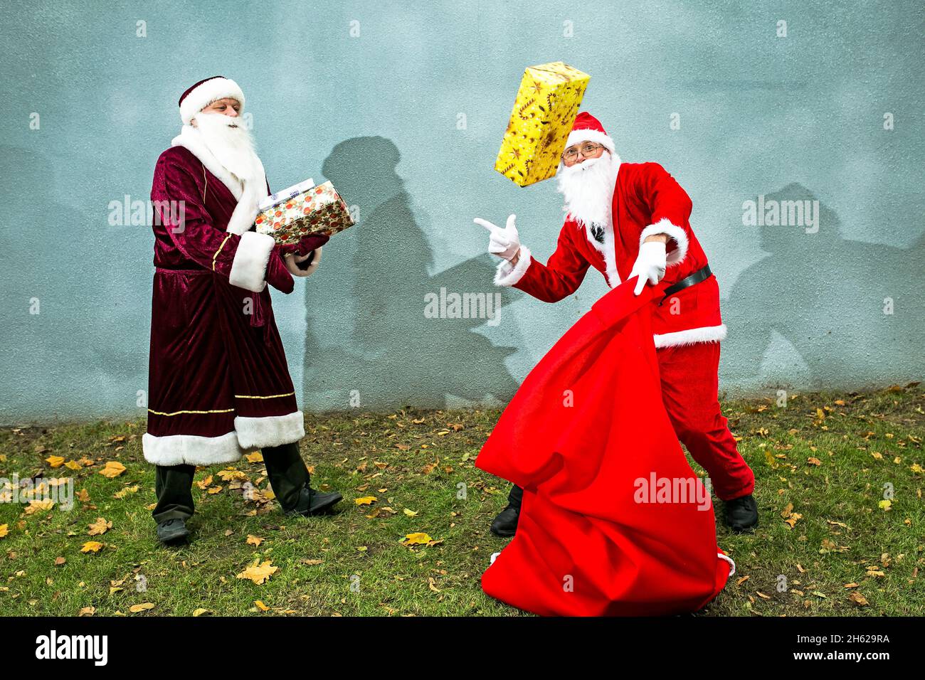 Two merry Santa Clauses are filling a large red bag with gifts ...