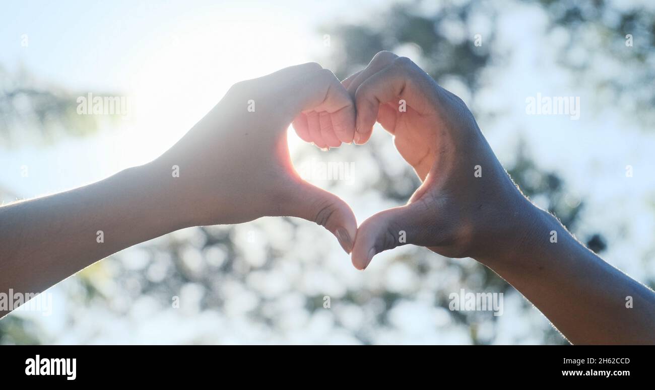 Unrecognizable couple catching setting sun with her heart shaped ...