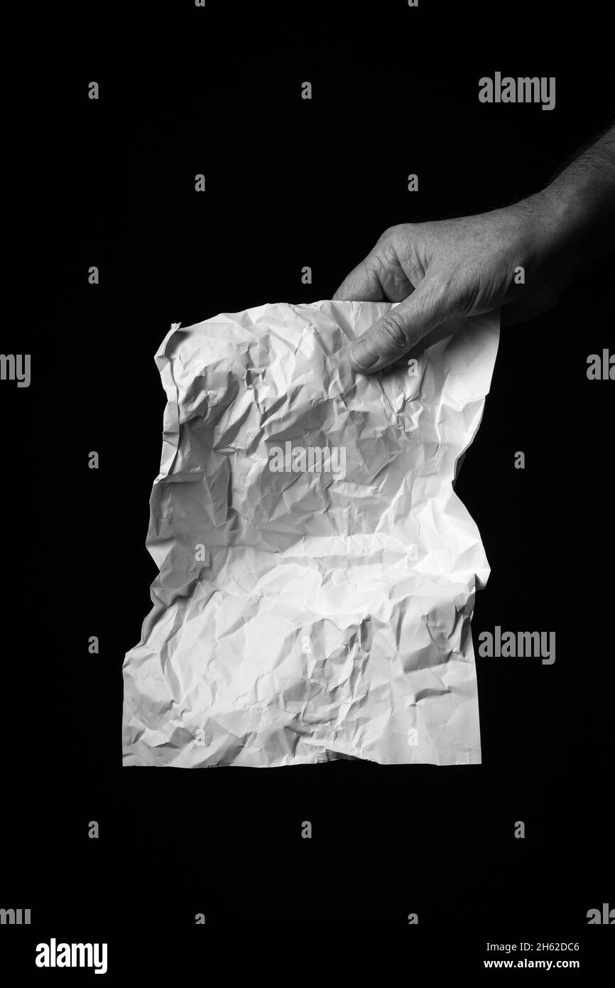 B+W image of male hand holding crumpled sheet of paper against black ...
