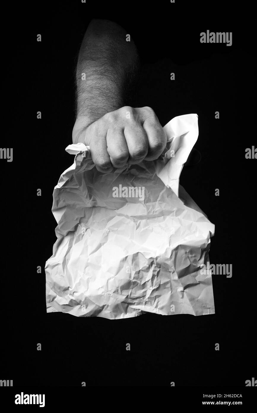 B+W image of clenched male hand holding crumpled sheet of paper against ...
