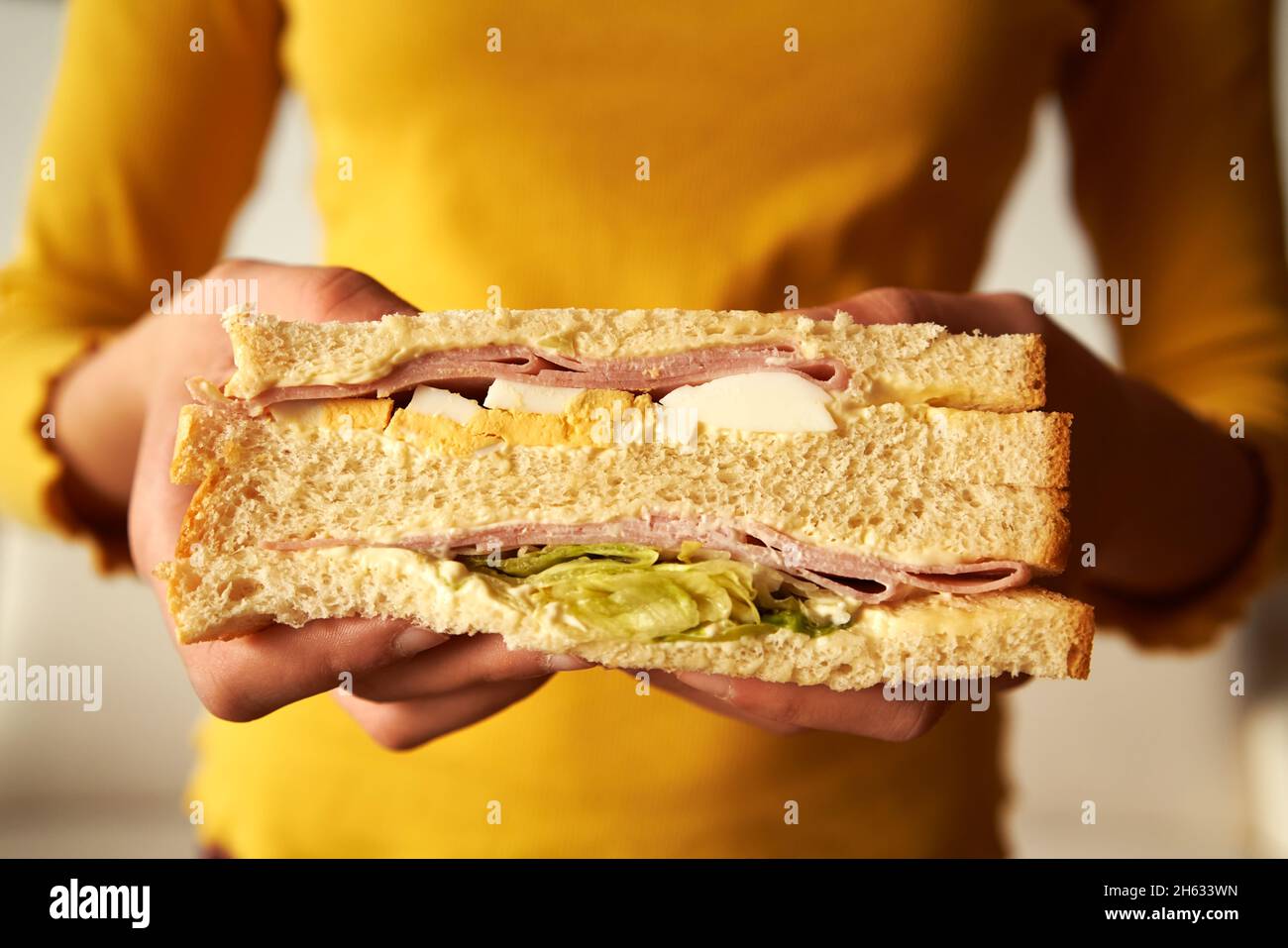 Sandwich with ham, eggs and lettuce held by the hands of a teenage girl ...