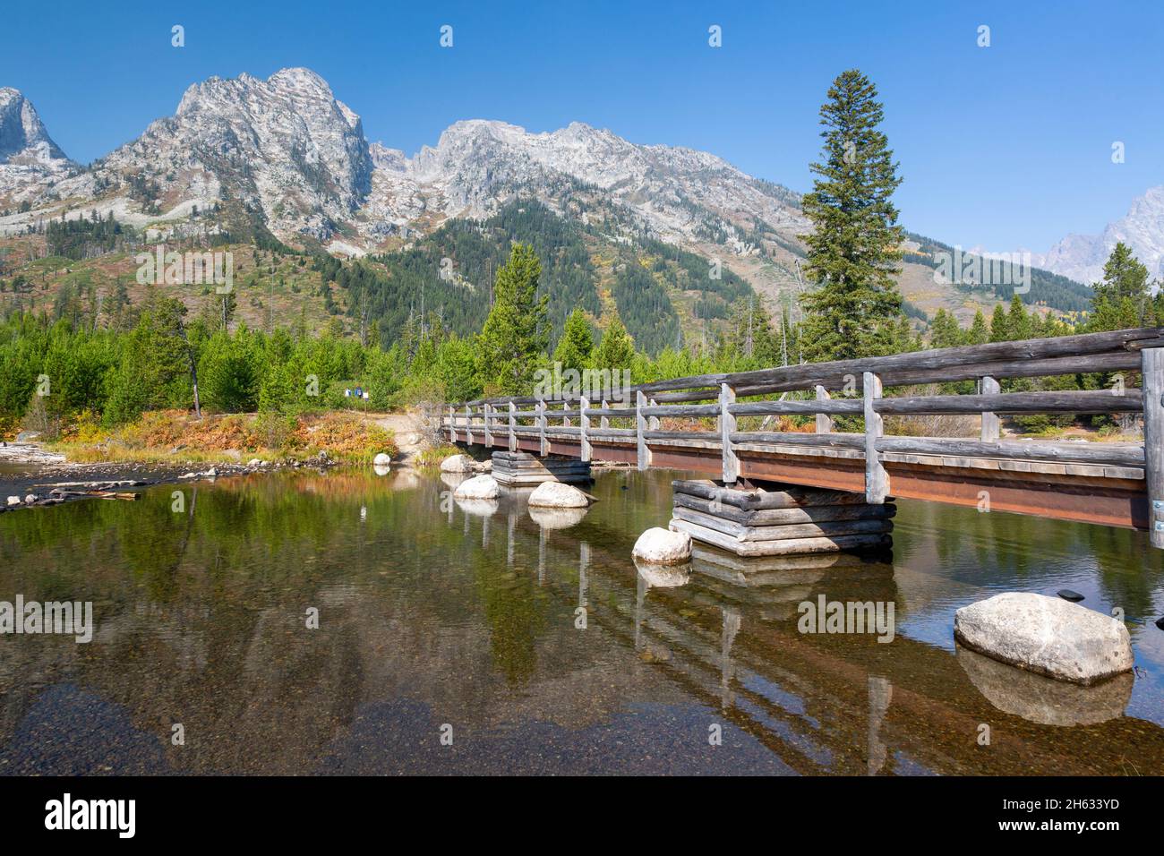 A small wooden hiking bridge crossing a section of String Lake along ...
