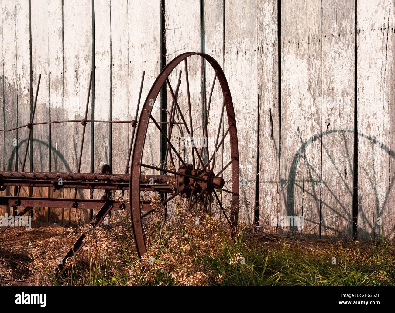 Late day light cast a shadow on old farm equipment by an old white ...