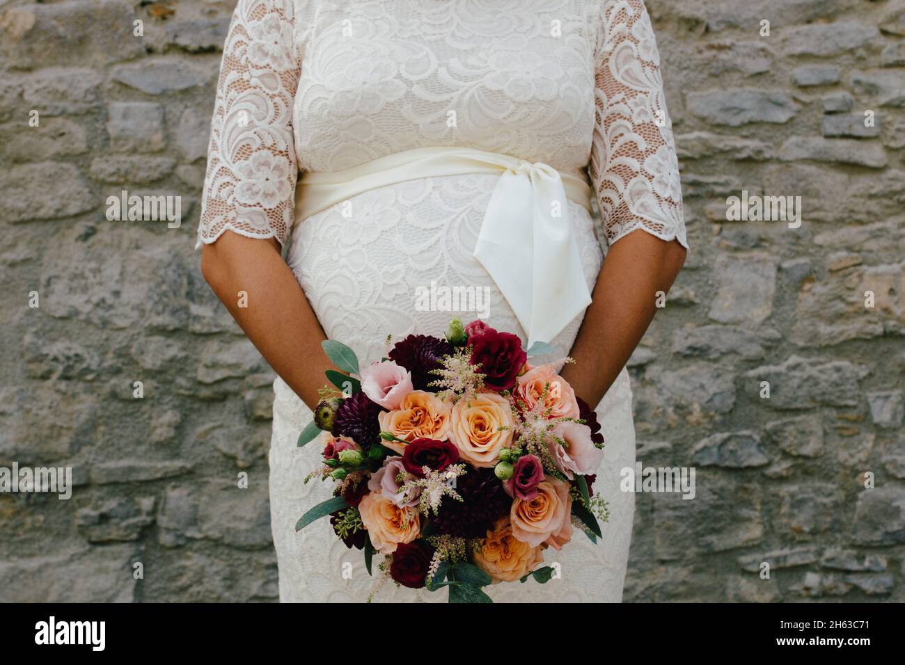 pregnant bride in a white lace dress with a colorful bridal bouquet in ...