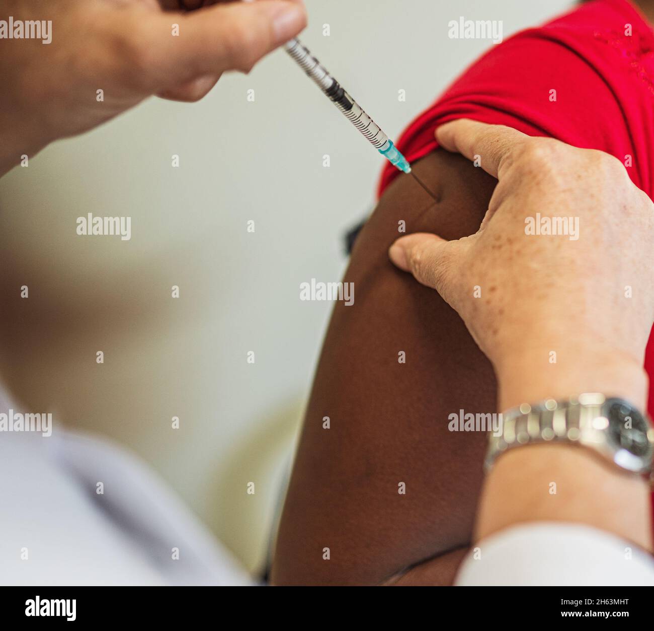 Latin female nurse giving shot or vaccine to a patient's shoulder ...
