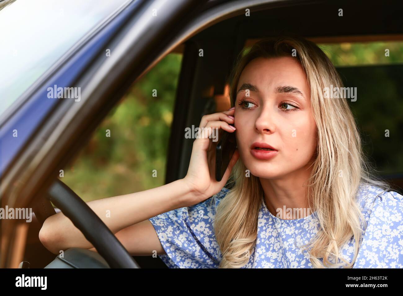 Young woman talking on a cell phone while sitting in the car in the ...