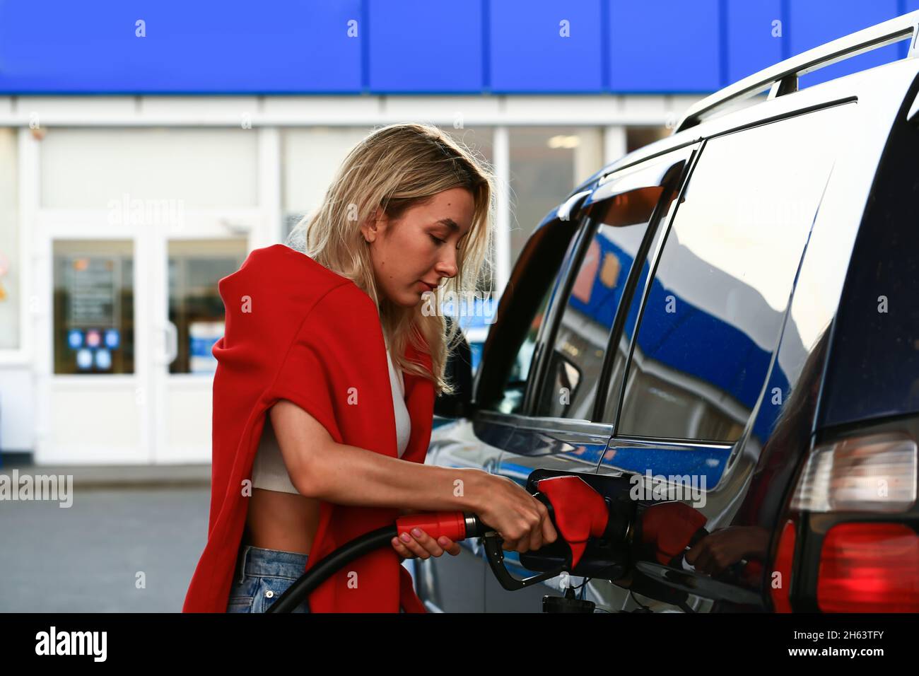Young woman refueling her car at a gas station. Attractive blonde ...