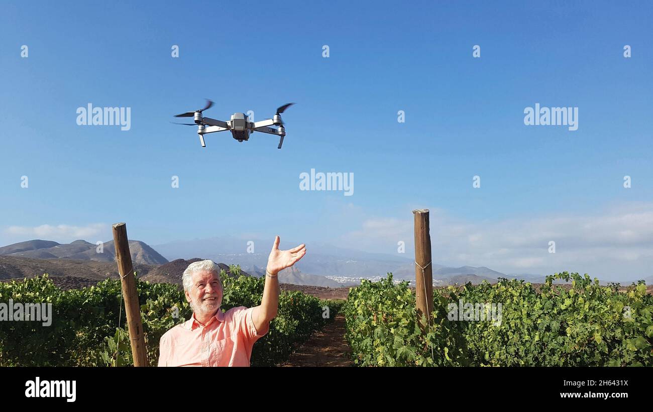 drone flying over field with senior man raising hand to catch it ...