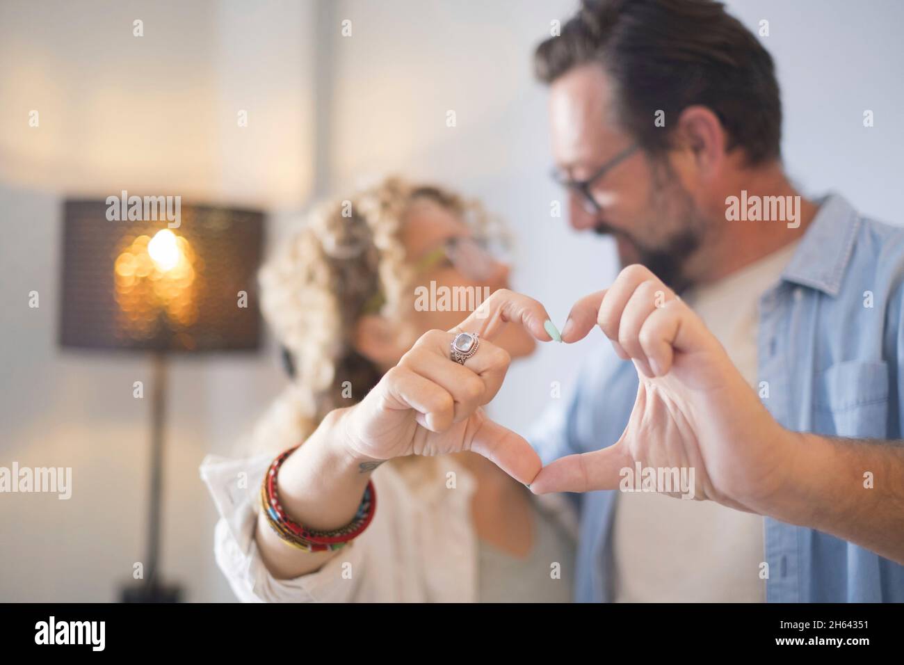 cheerful couple embracing while doing heart shape gesture with hands ...