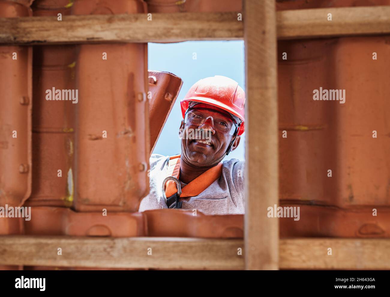 Latin worker installing yellow ceramic roofing tiles mounted on wooden ...