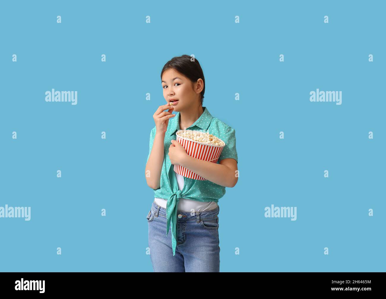 Cute girl eating popcorn on blue background Stock Photo - Alamy