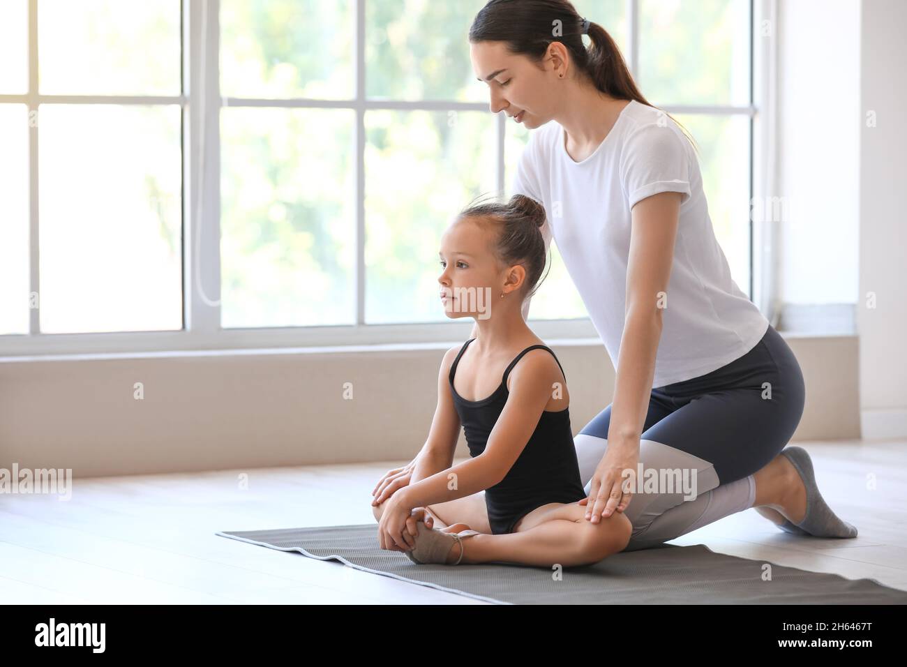 Coach helping little girl to do gymnastics in gym Stock Photo - Alamy