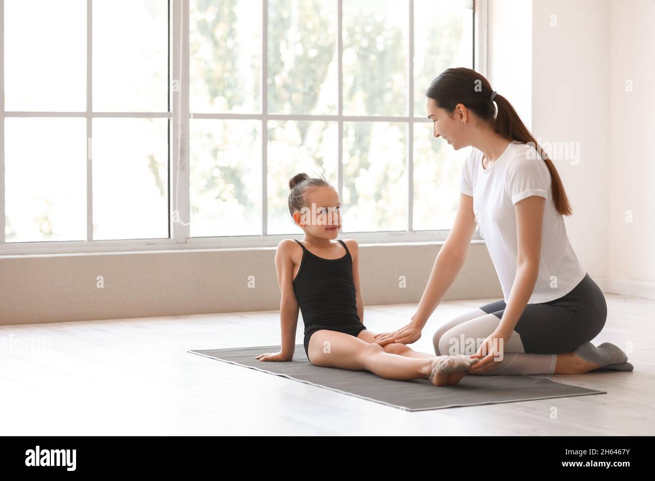 Coach helping little girl to do gymnastics in gym Stock Photo - Alamy