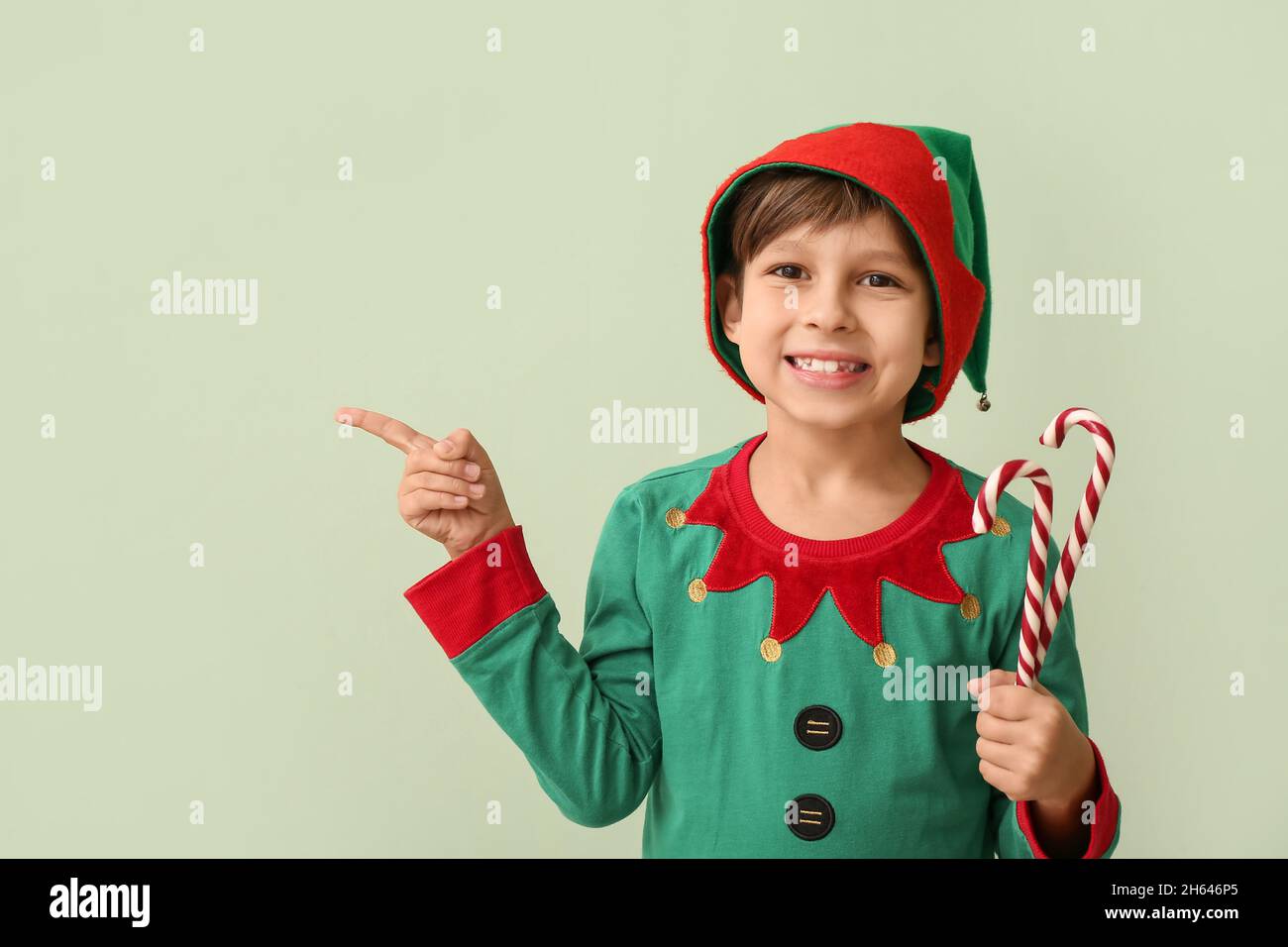 Cute little elf with candy canes pointing at something on color ...