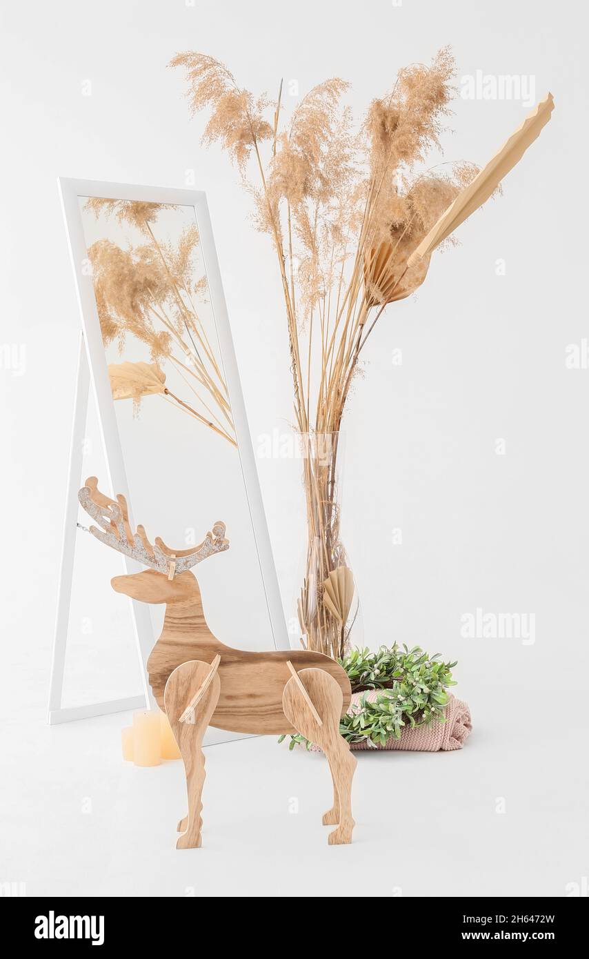 Wooden reindeer, Christmas wreath, vase with reed flowers and mirror on ...