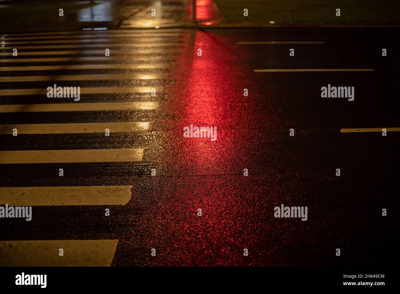 The red color of the traffic light is reflected on the pedestrian ...