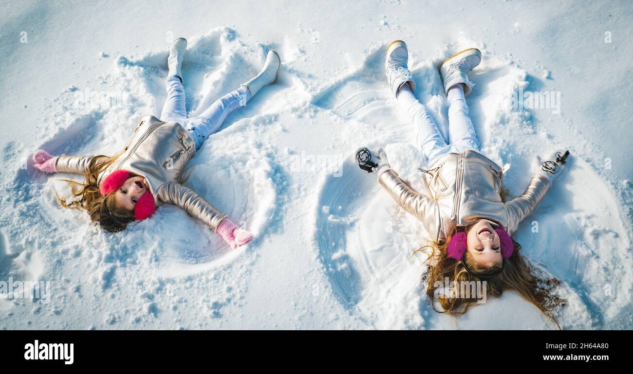 Two little girl making snow angel while lying on snow. Happy children ...