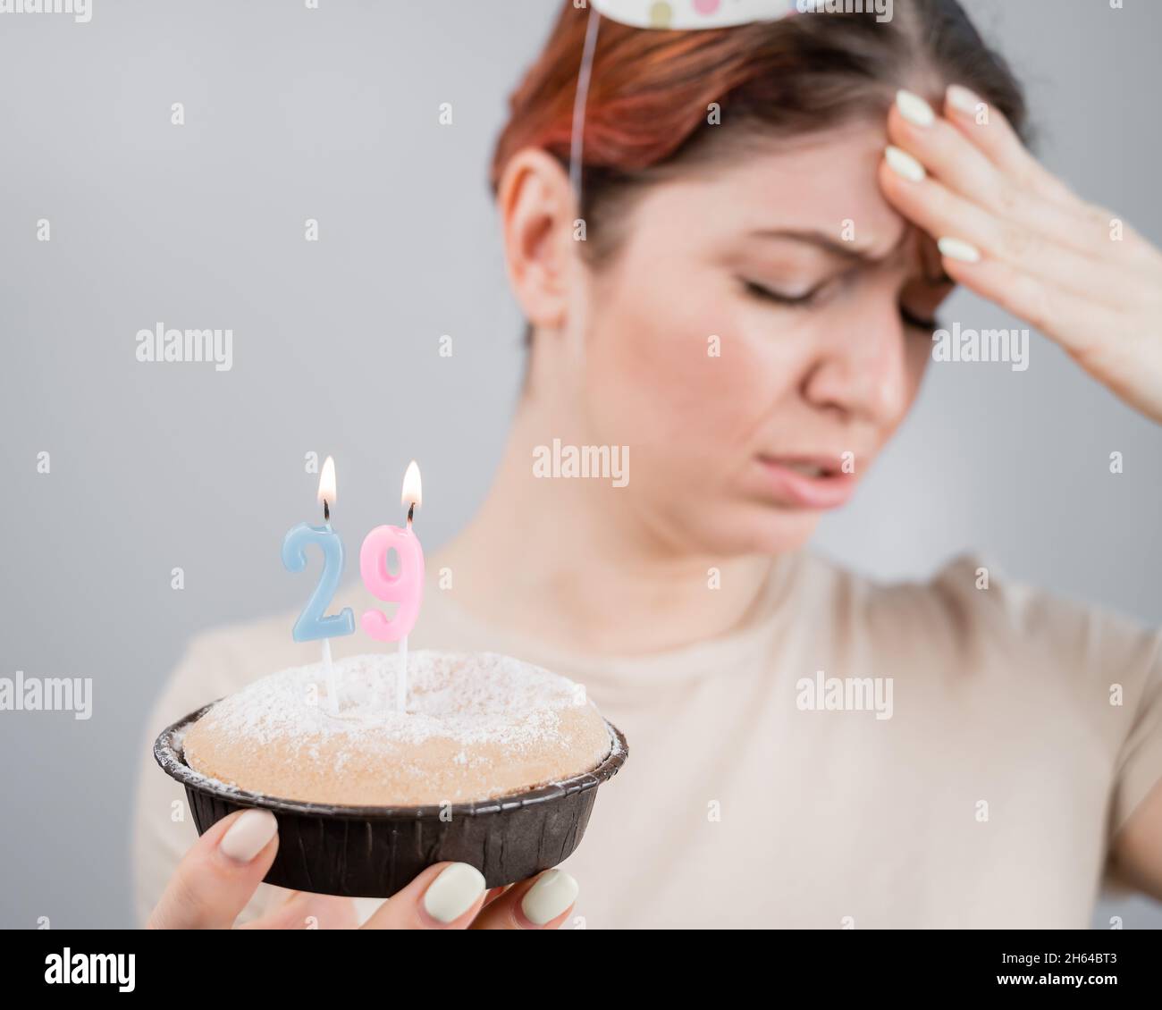 Unhappy woman holding a cake with candles for her 29th birthday. The ...