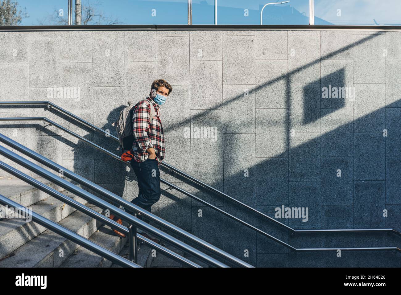 Young man wearing a protective mask on his face walking down the stairs ...