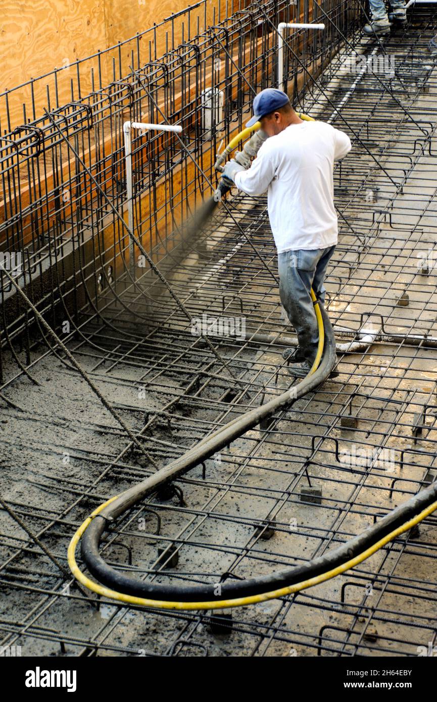 Construction worker spraying shotcrete over reinforcement steel to form ...