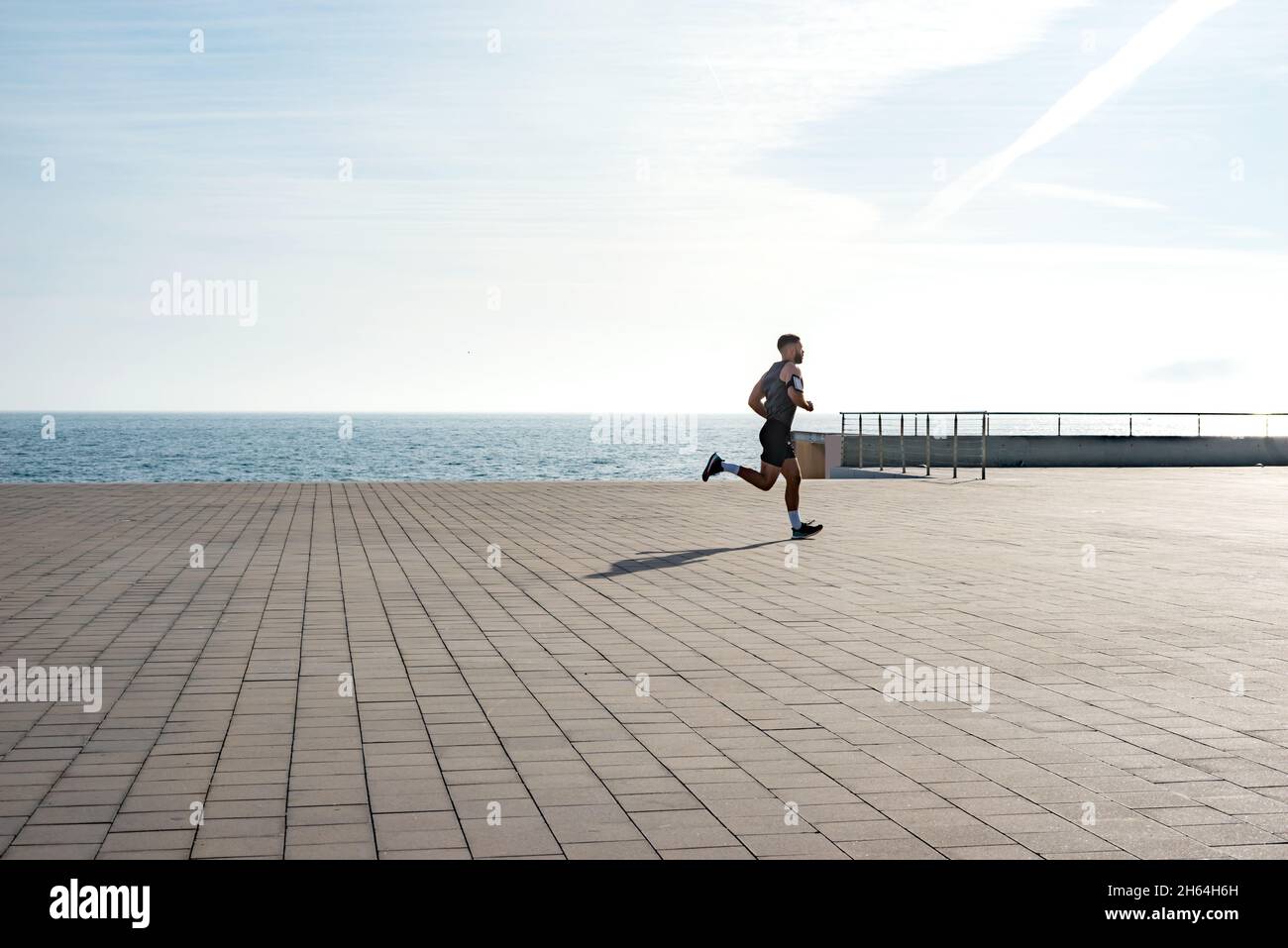 Fit young man running along seafront. Male runner jogging early in the ...