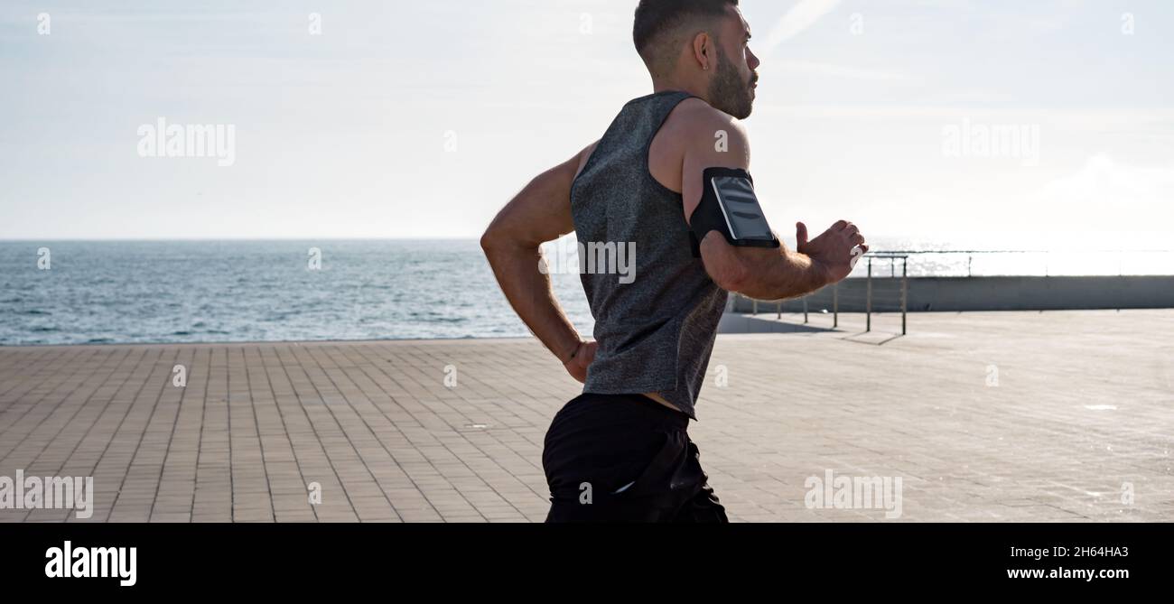 Fit young man running along seafront. Male runner jogging early in the ...