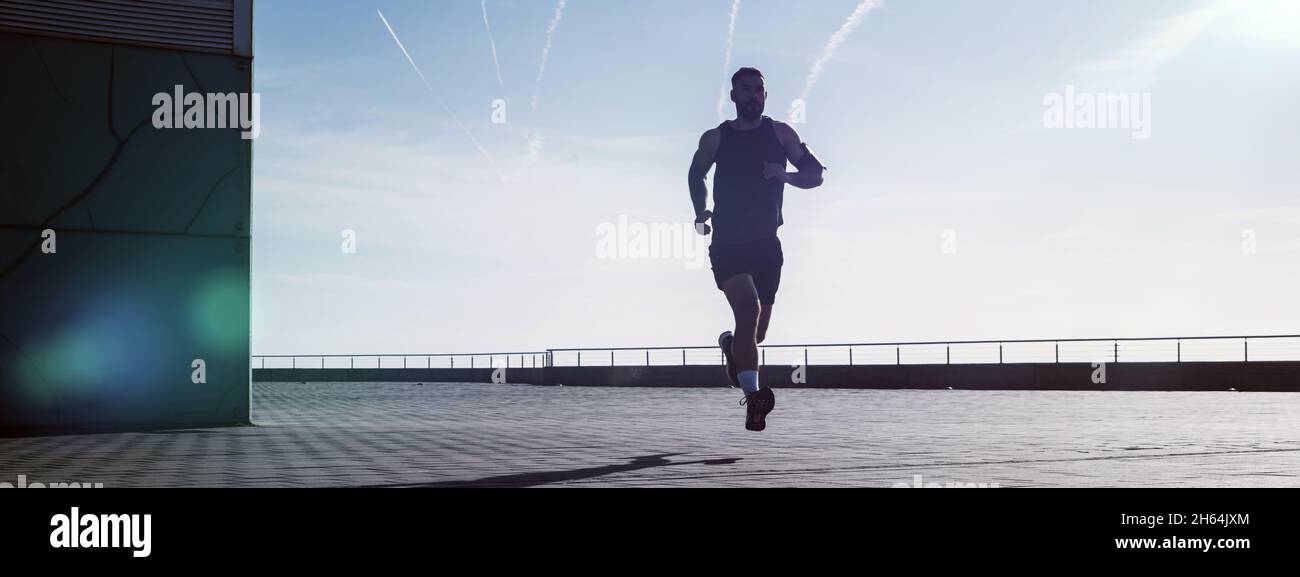 Fit young man running along seafront. Male runner jogging early in the ...