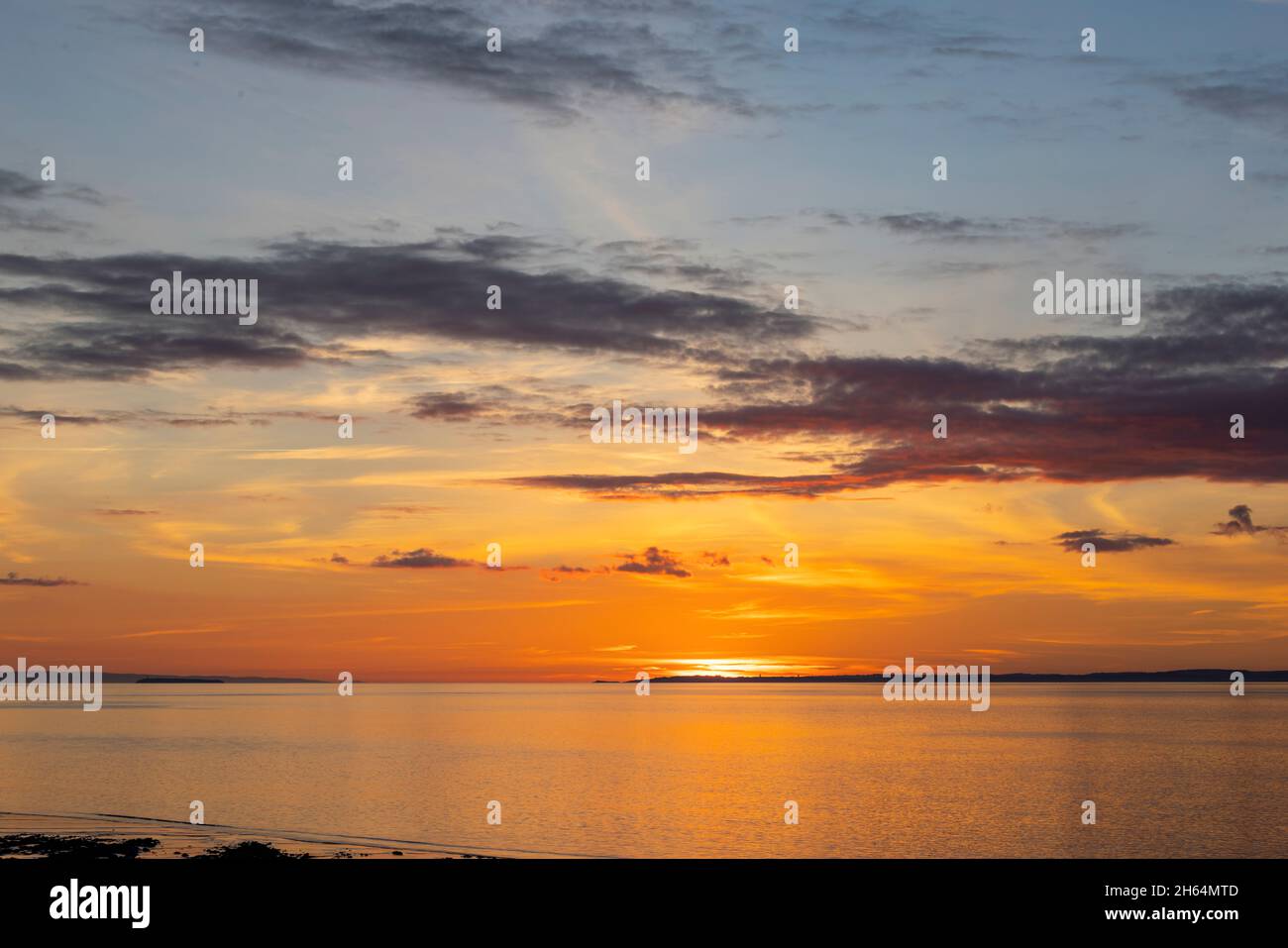 The setting sun lighting up the sky and reflecting onto a calm sea ...