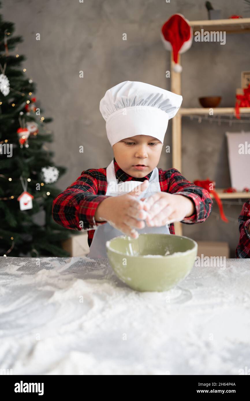 Children are cooking for Christmas. Boy baker in a cap and apron kneads ...