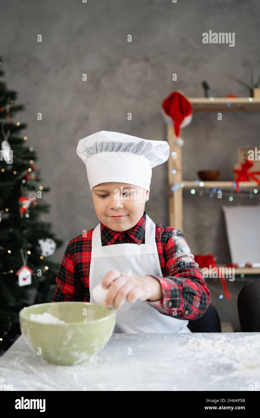boy baker in white baker's uniform prepares dough for Christmas cookies ...