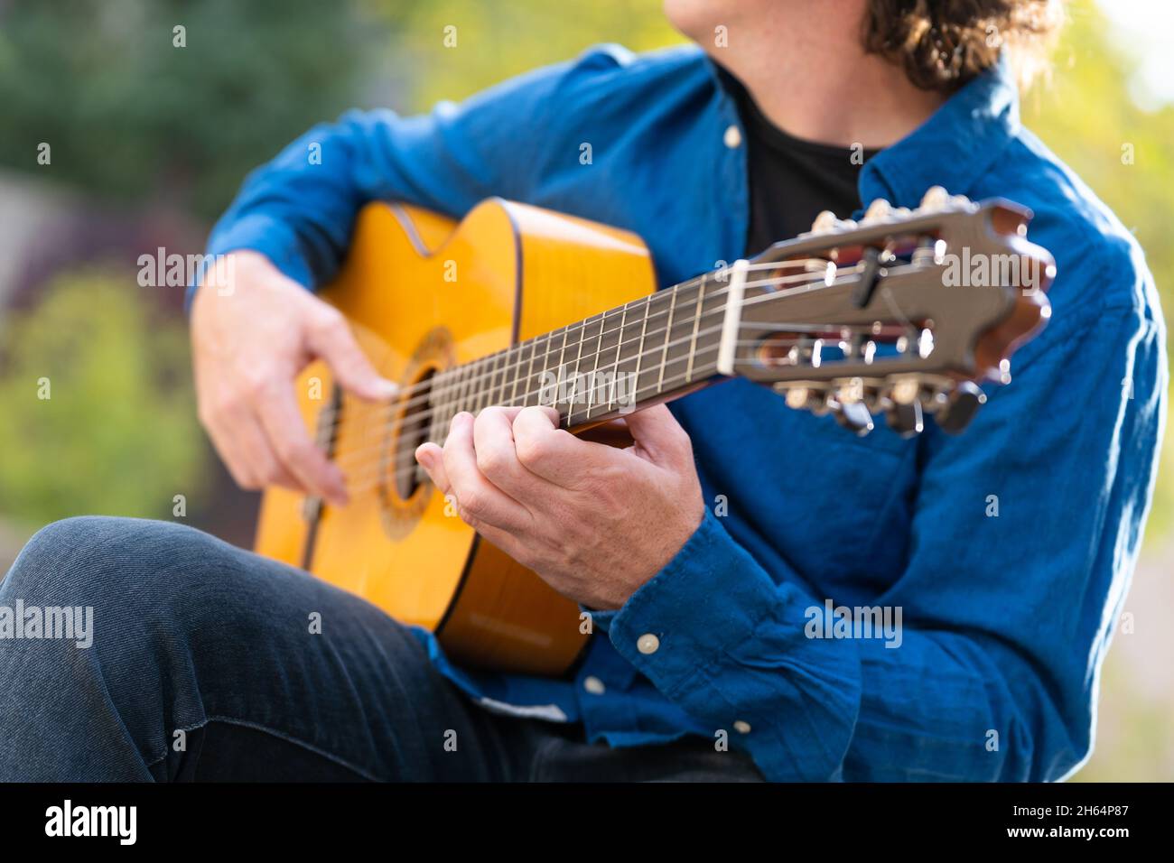 Unrecognizable middle-aged man playing Spanish guitar sitting on park ...