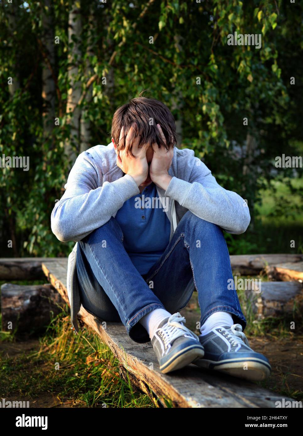 Sad Young Man sit on the Log outdoor Stock Photo - Alamy
