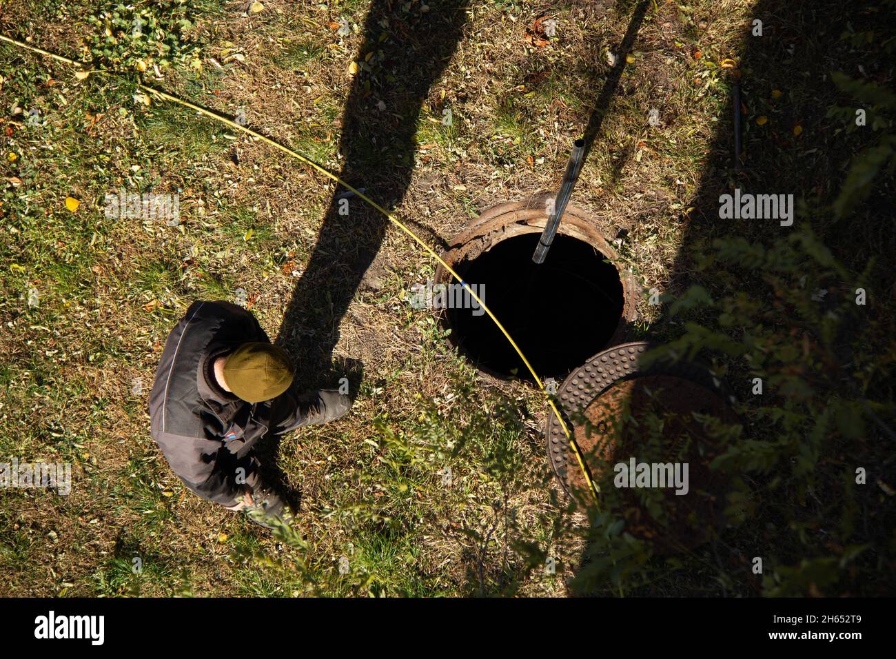 Worker in a uniformed near an open sewer hatch. Yellow electric cable ...