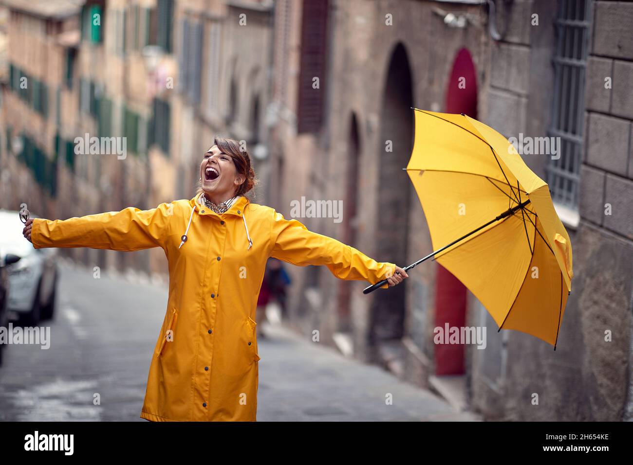 A young excited and cheerful girl with a yellow raincoat and umbrella ...