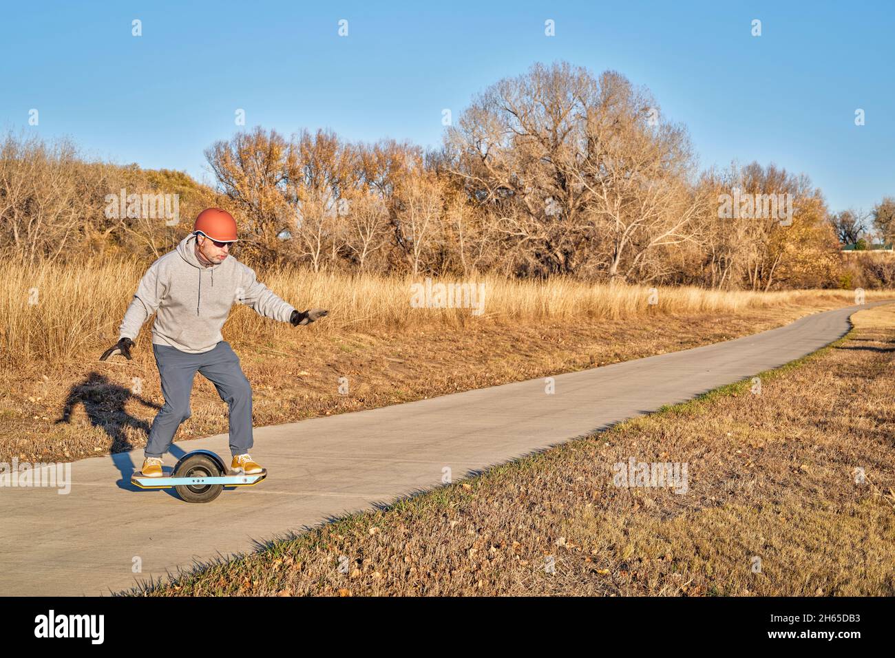 senior man is riding one-wheeled electric skateboard on a paved bike ...
