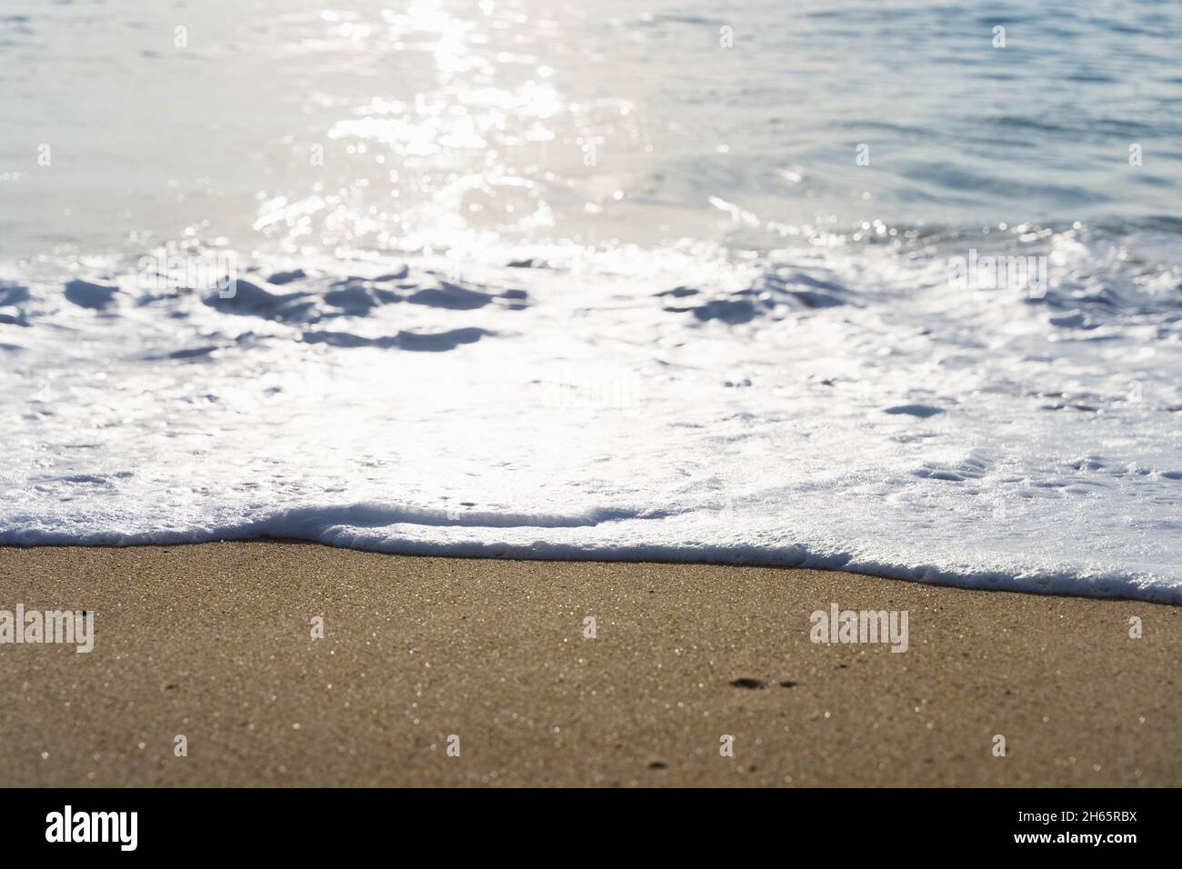 Sun reflection on sea water as wave reaches shore by sand on the beach ...