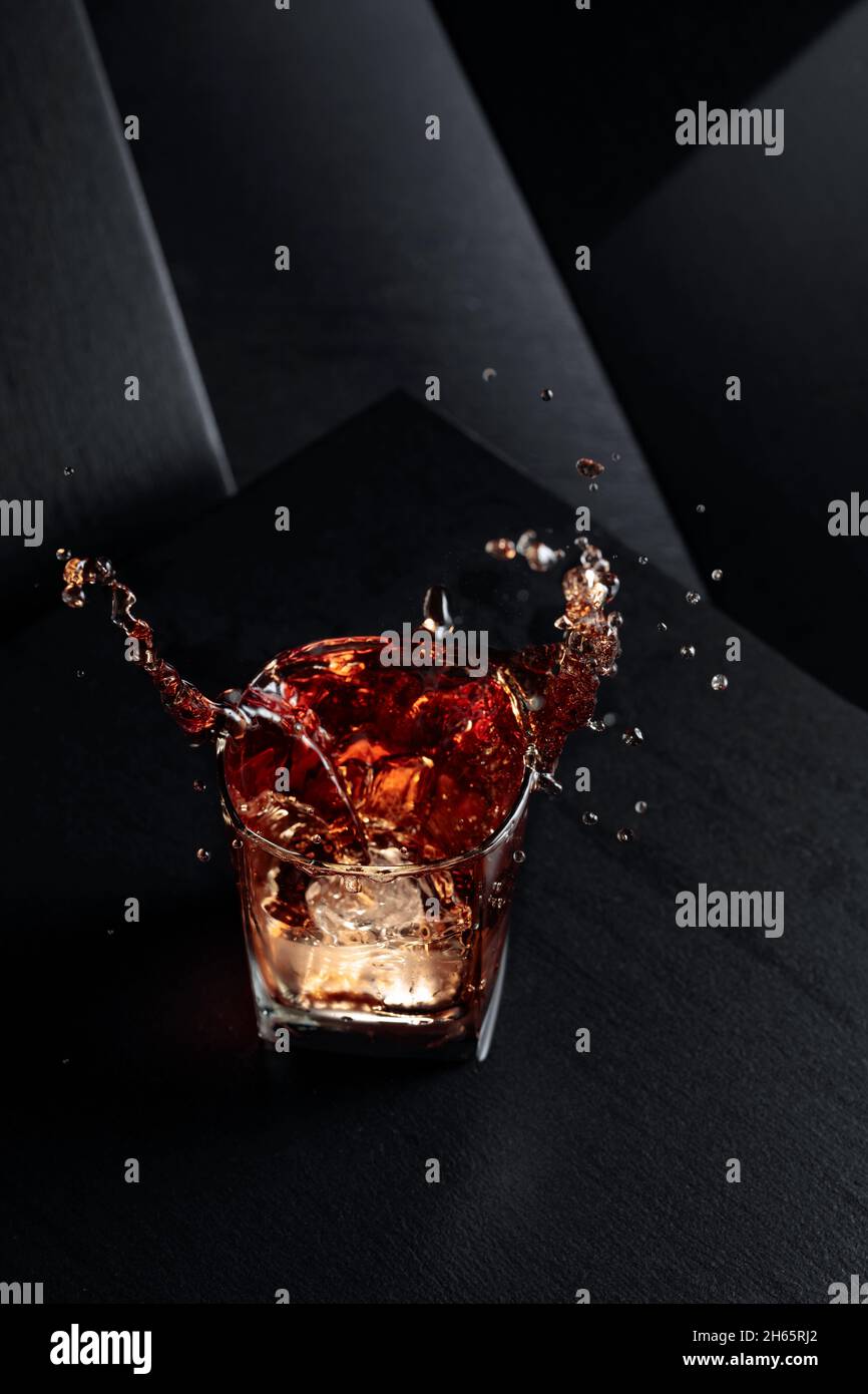 Ice cubes fall into a glass of whiskey creating splashes Stock Photo - Alamy