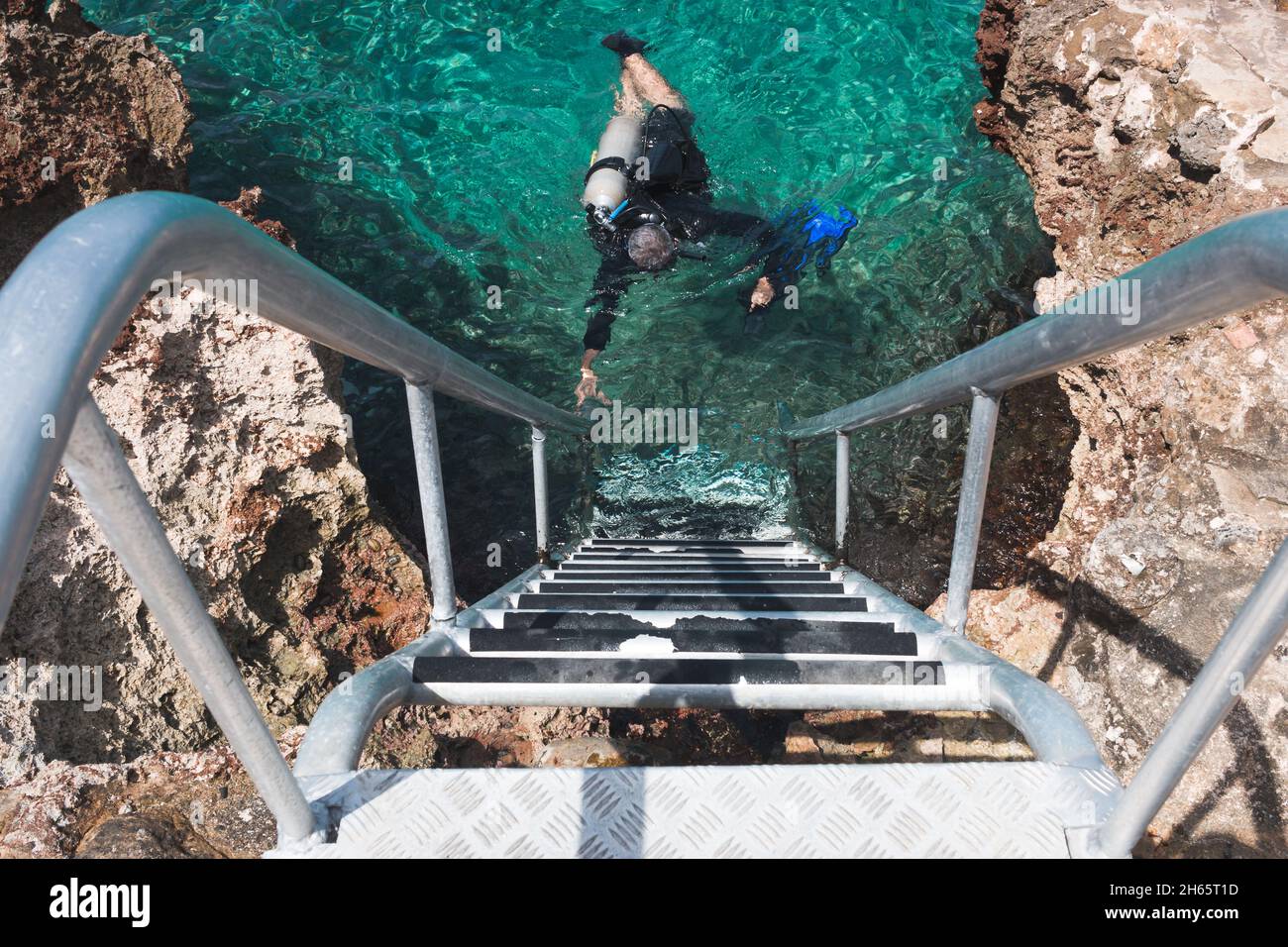 Male scuba diver floating in crystal clear teal water next to staircase ...