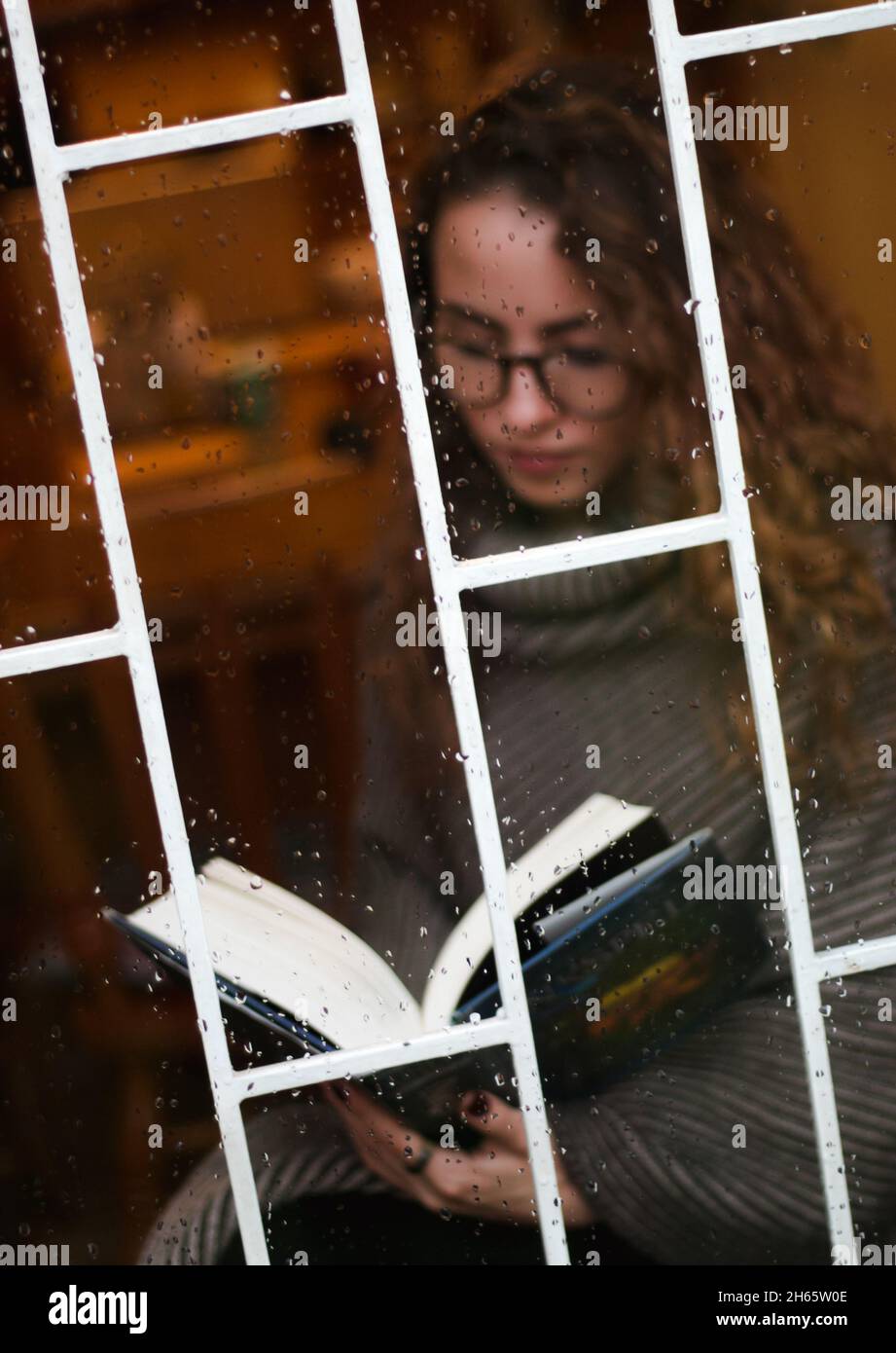 Beautiful, warm portrait through window with drops of water of young ...