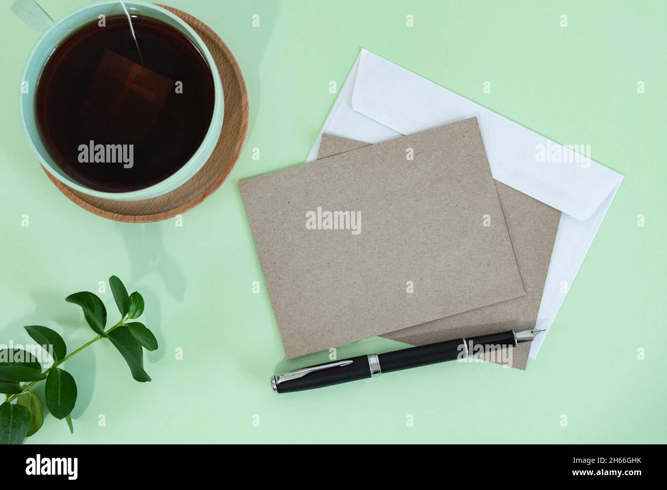 A cup of tea, envelope, pen, and paper sheets on a modern green office ...