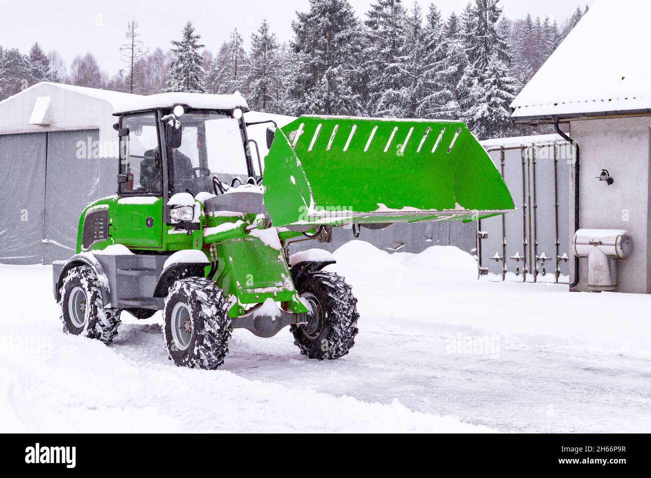 Little green tractor with snowplow removing snow during snowfall ...