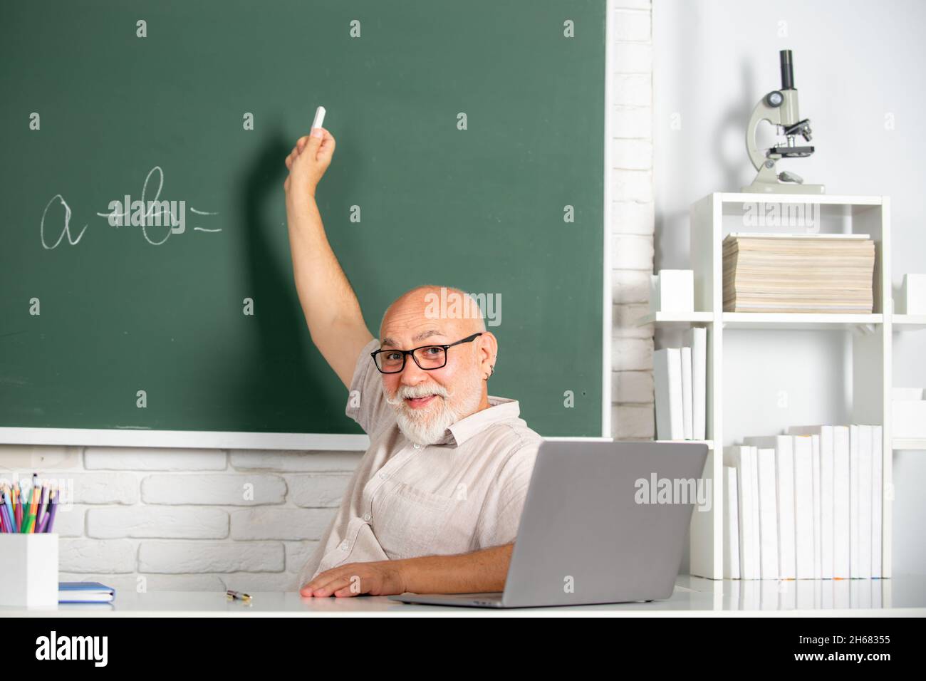 Senior teacher in the classroom on blackboard background. Old professor ...