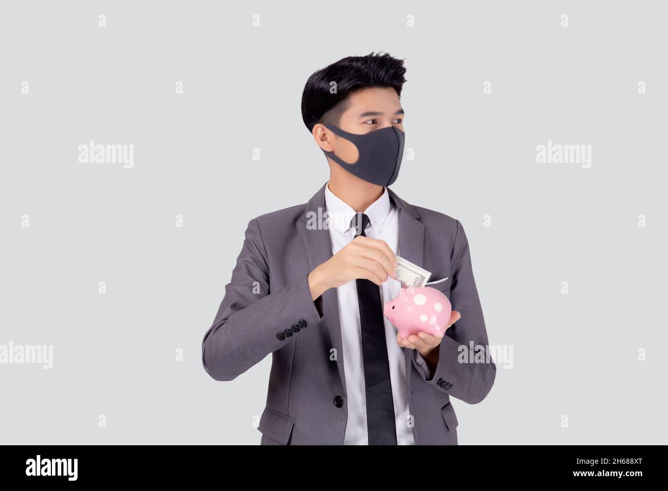 Young asian businessman in face mask holding money dollar and piggy ...